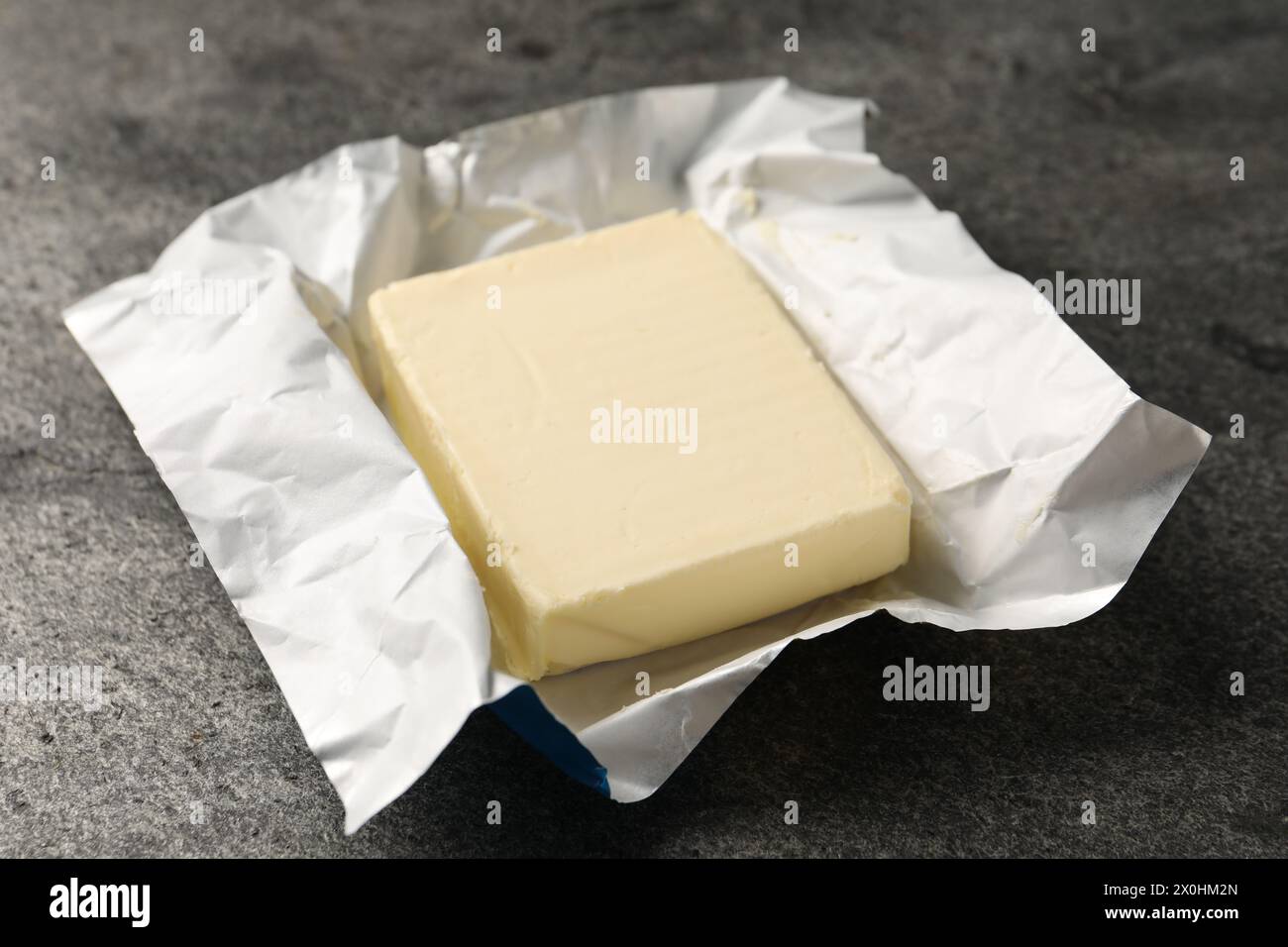 Block of tasty butter in open foil packaging on grey table, closeup ...