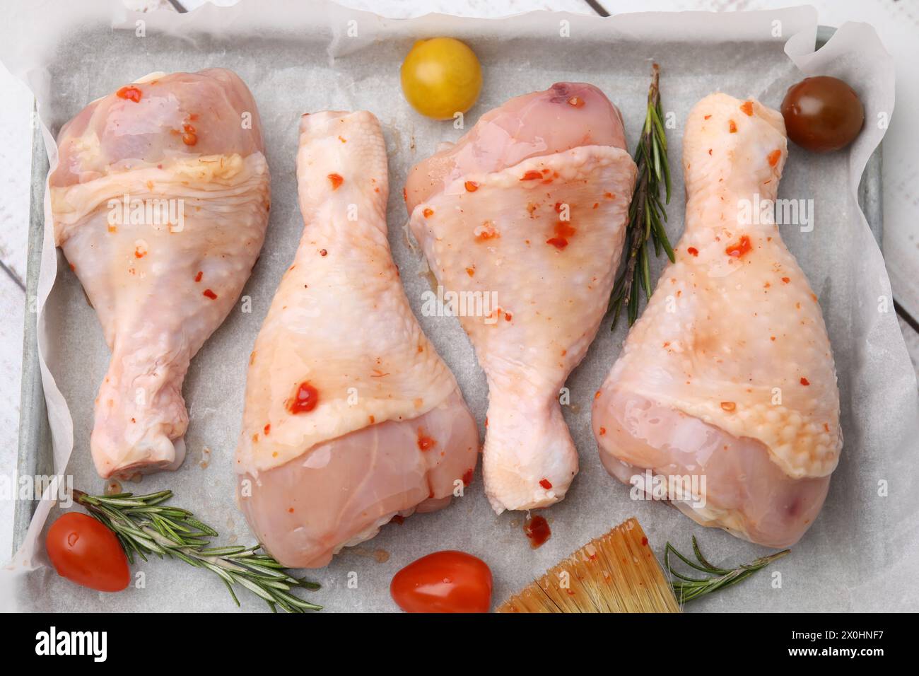 Raw marinated chicken drumsticks, rosemary and tomatoes in baking dish ...