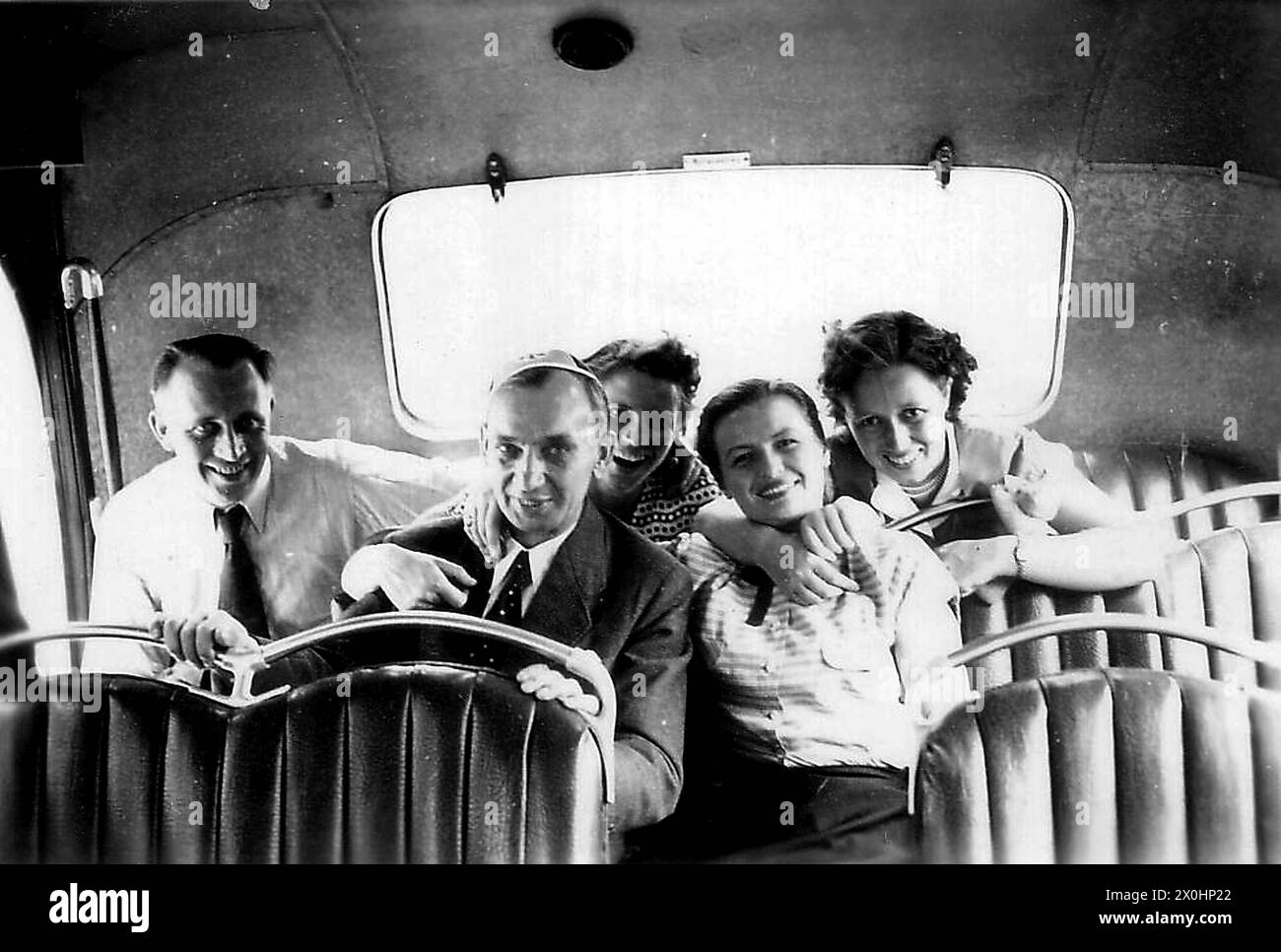 Two men and three women sit smiling in a bus during a company outing in ...