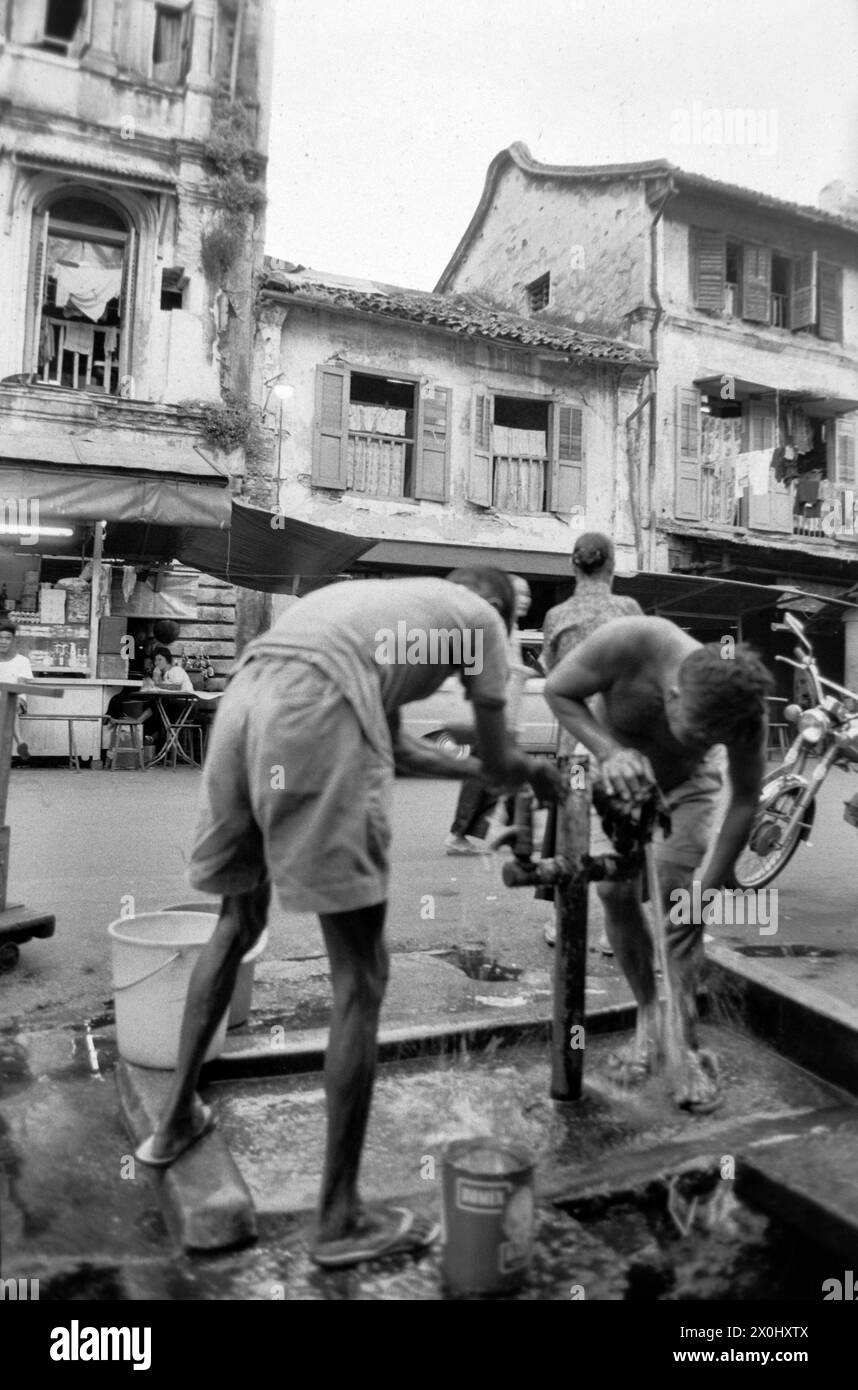 Two men are standing by a well on a road. A muddy puddle has formed ...