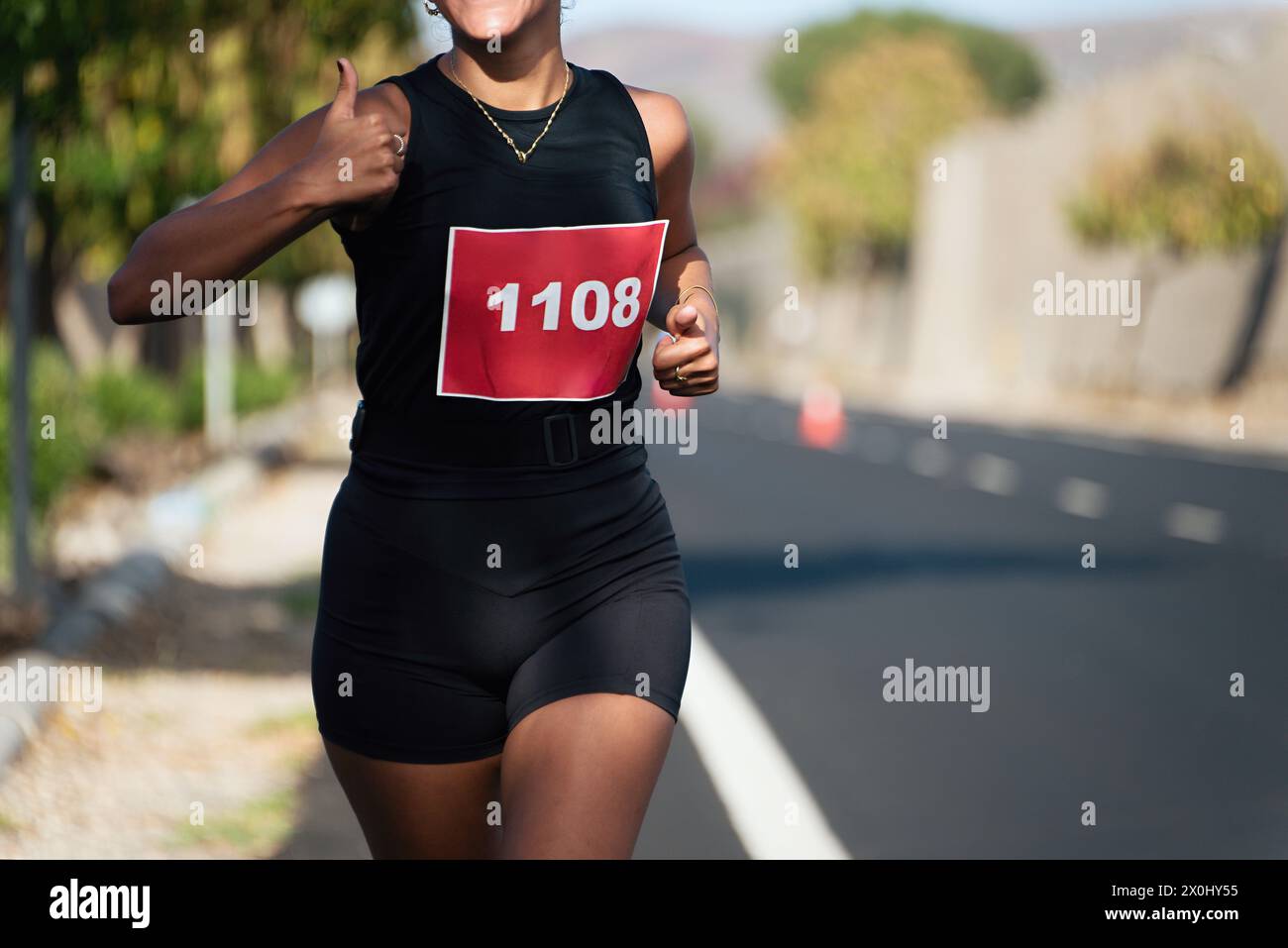Marathon runner woman gesturing thumbs up outdoors in a city outskirts ...