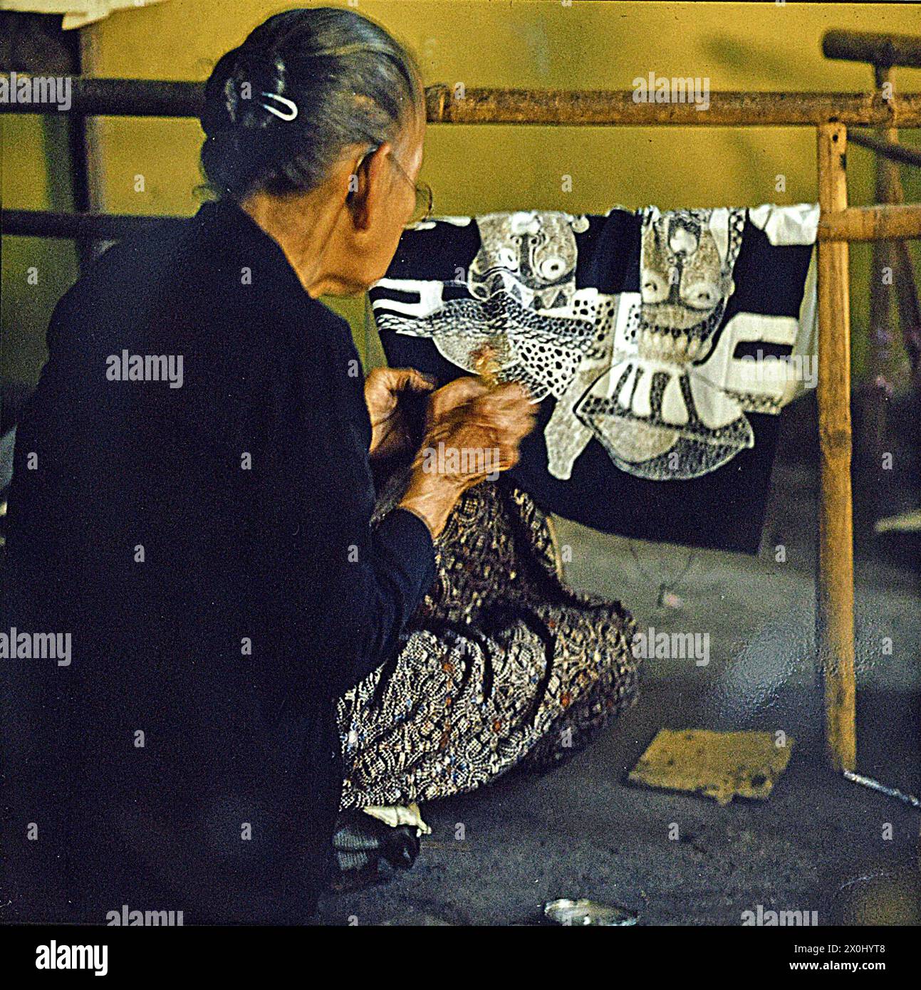 An elderly woman is sitting on the floor of a hut with her back to the ...