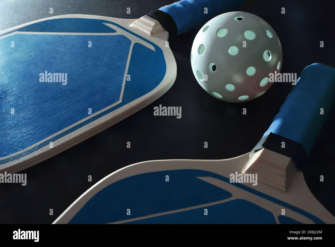 Two blue wooden paddle pickleball rackets and a white ball on black ...