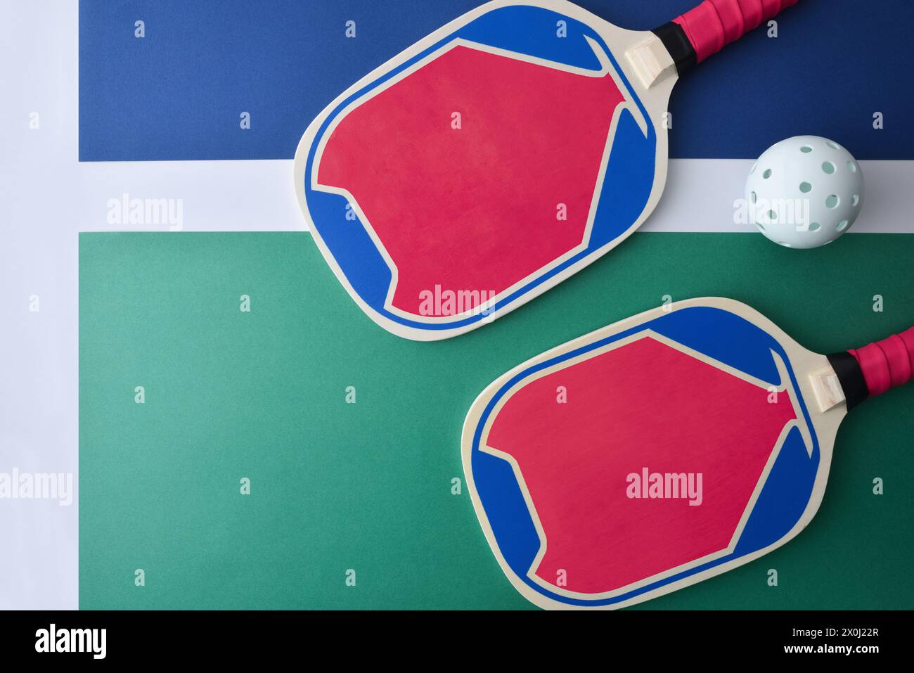 Blue and pink wooden pickleball paddles and a white ball on playing ...