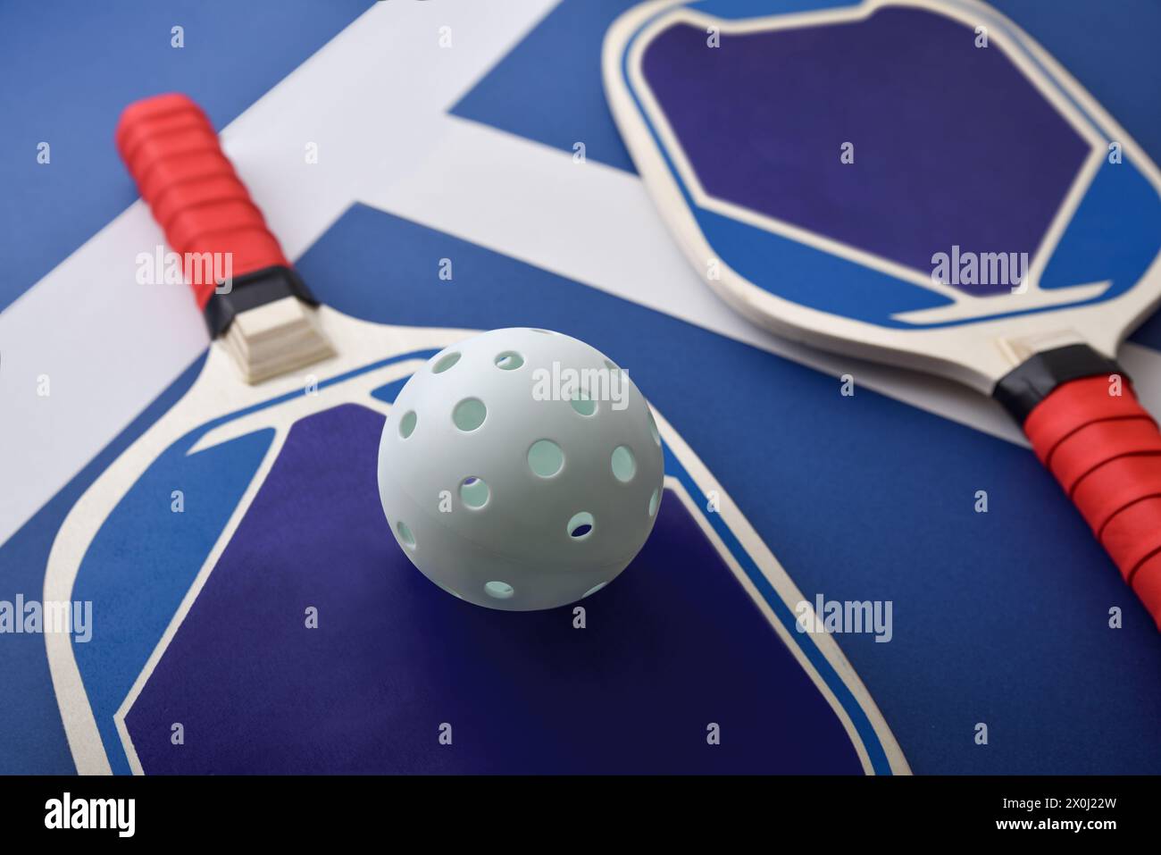 Blue and red wooden pickleball paddles and a white ball on blue playing ...