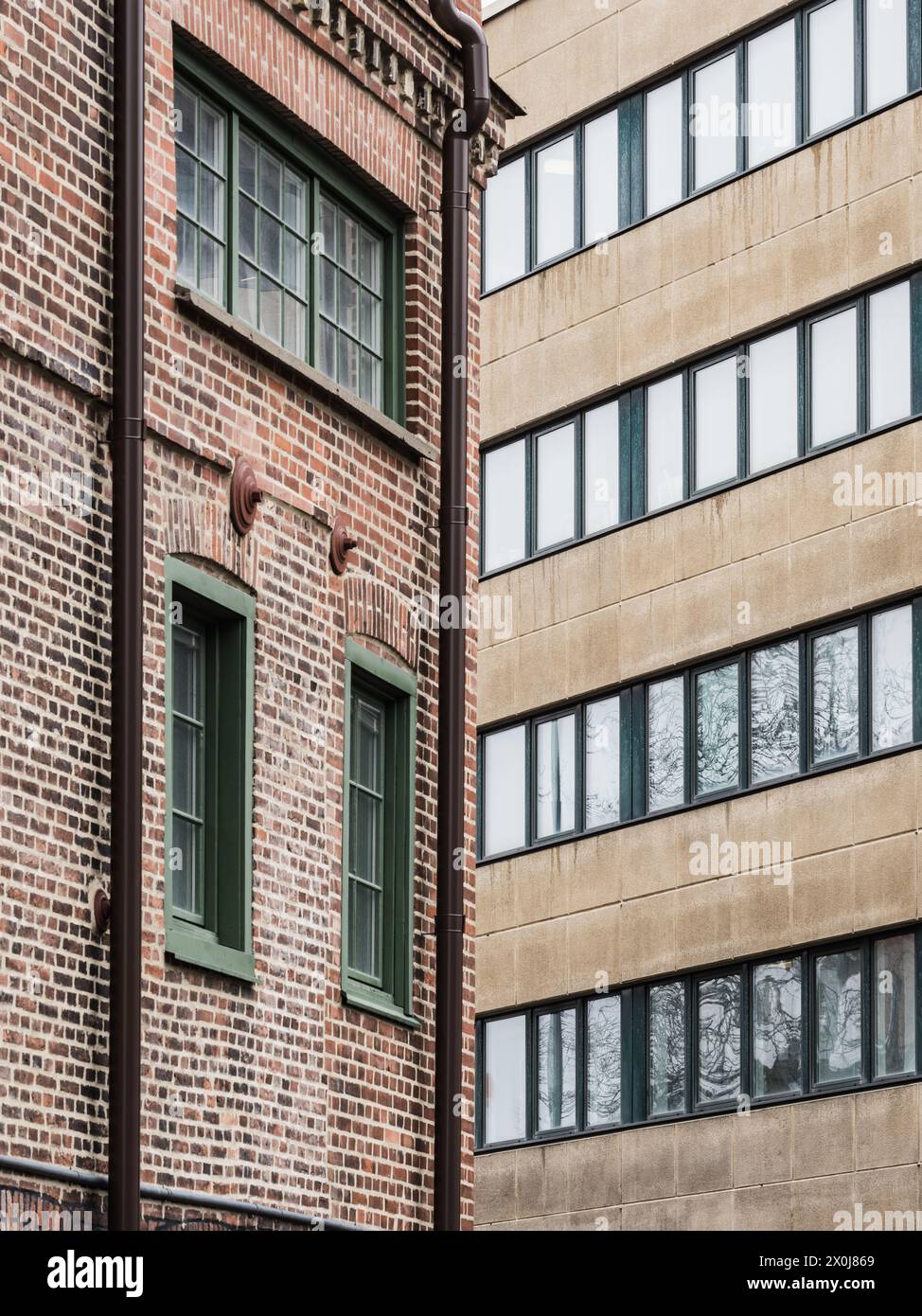 A tall brick building with green windows stands next to a sleek modern ...