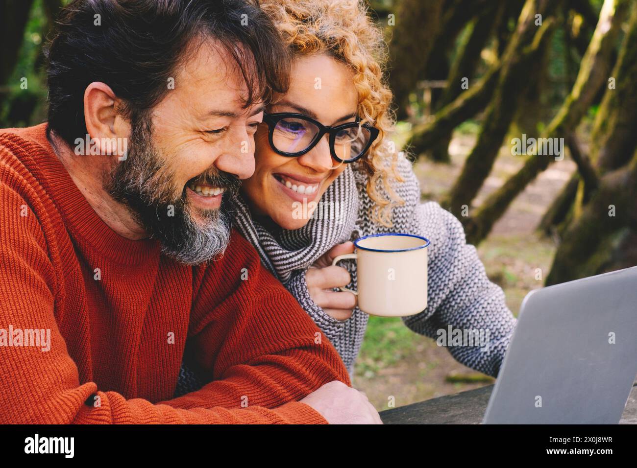 Happy modern couple use together laptop computer outdoors with trees ...