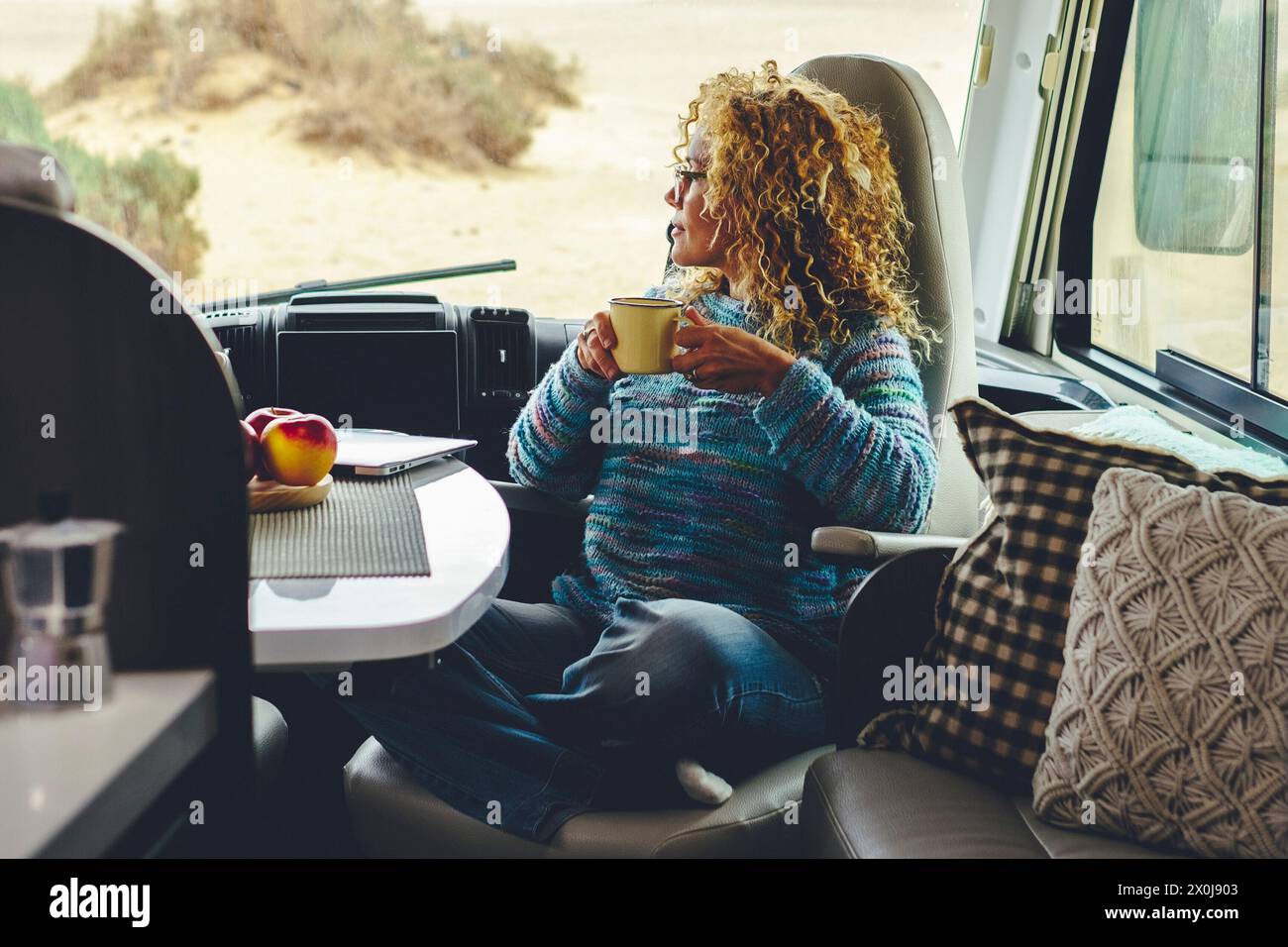 Adult nice woman sitting with a coffee cup in a camper van and looking ...