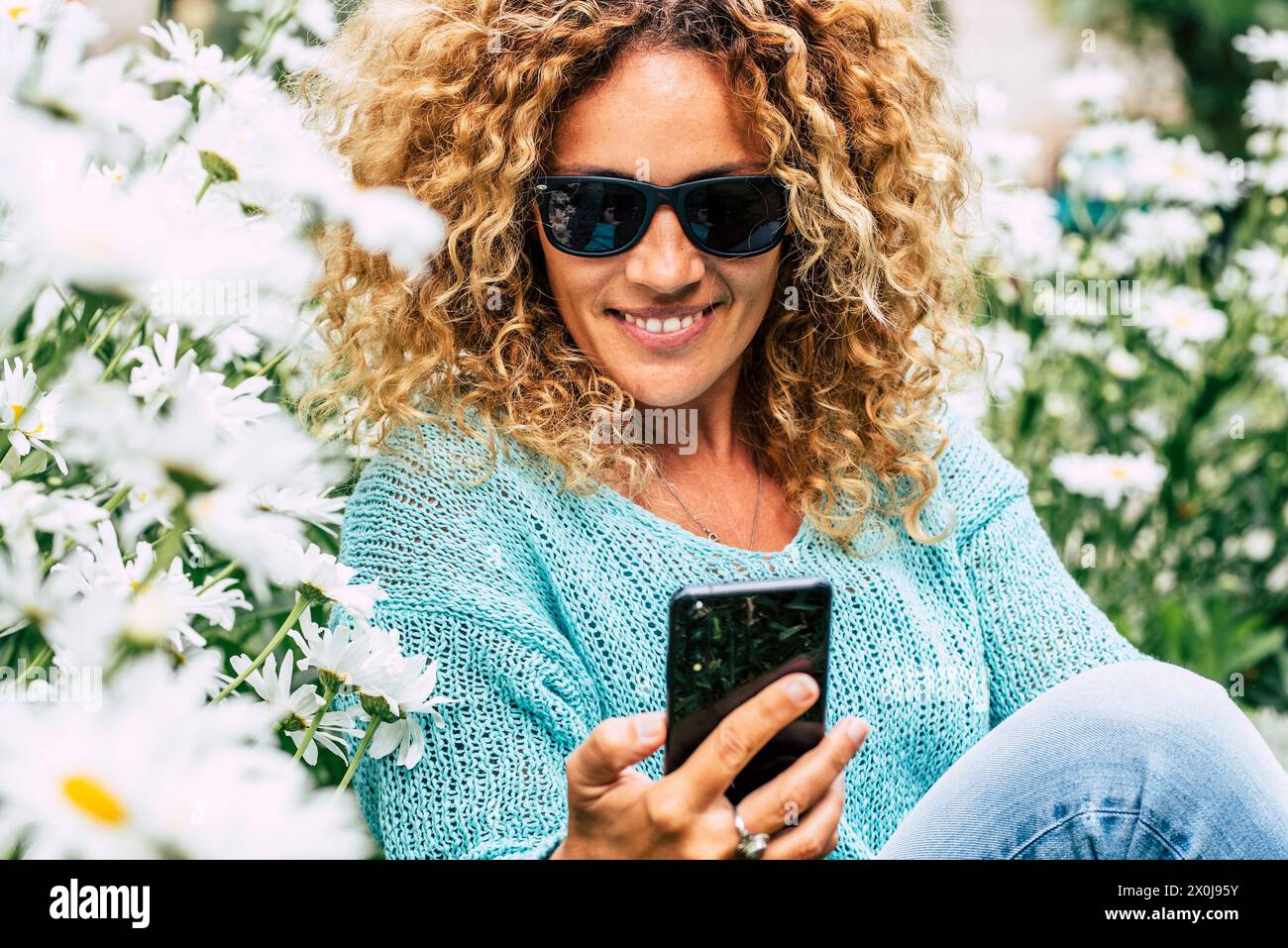 Cute caucasian woman using mobile phone outdoor sitting with daisies ... Cute caucasian woman using mobile phone outdoor sitting with daisies ...