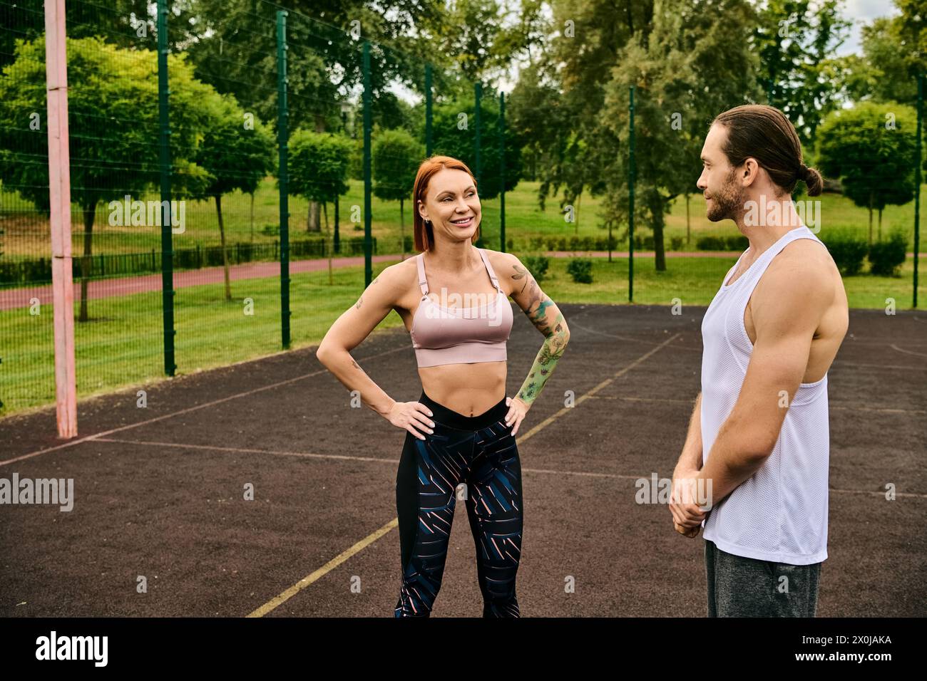 A man and a woman in sportswear stand ready on a tennis court ...