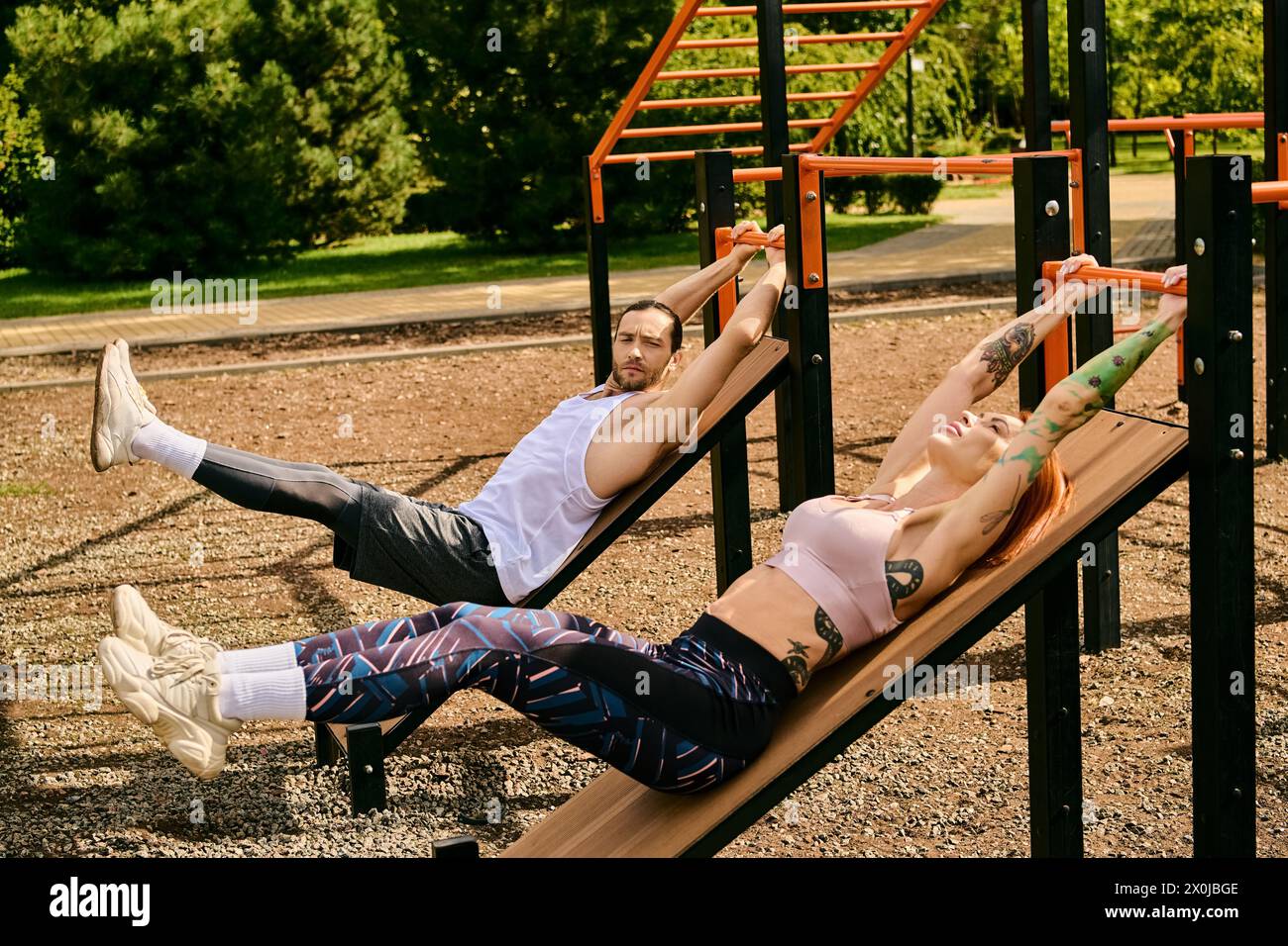 A man and woman in sportswear are laying down on a bench outdoors ...