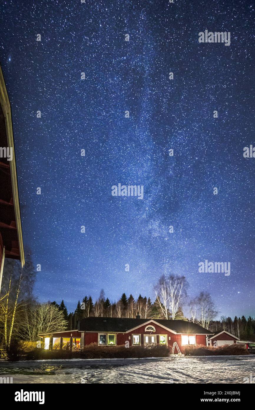 The Milky Way in the blue sky directly above a red Swedish wooden house ...