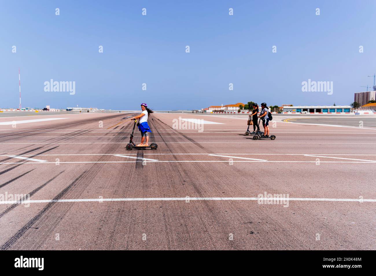 Women riding an electric scooter across the runway to cross between ...