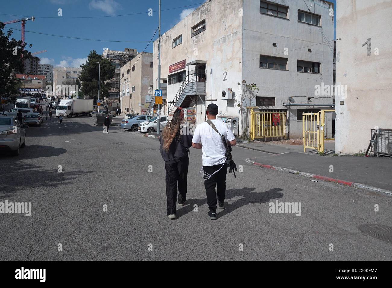 A religious Jew with an assault rifle slung across his back walks with ...