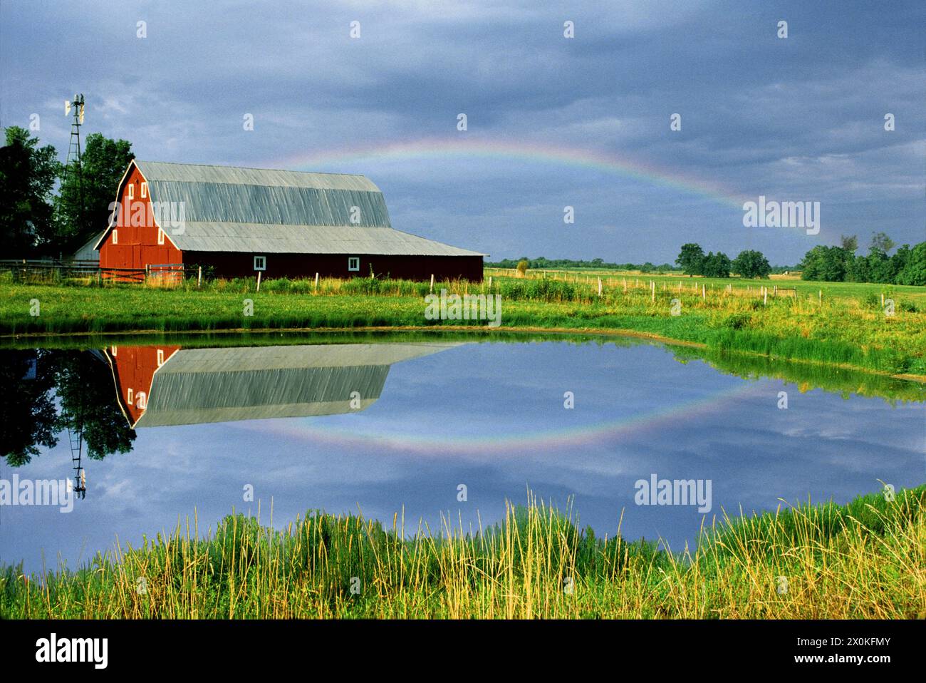 Classic midwestern barn with farm pond after a rain and a rainbow ...