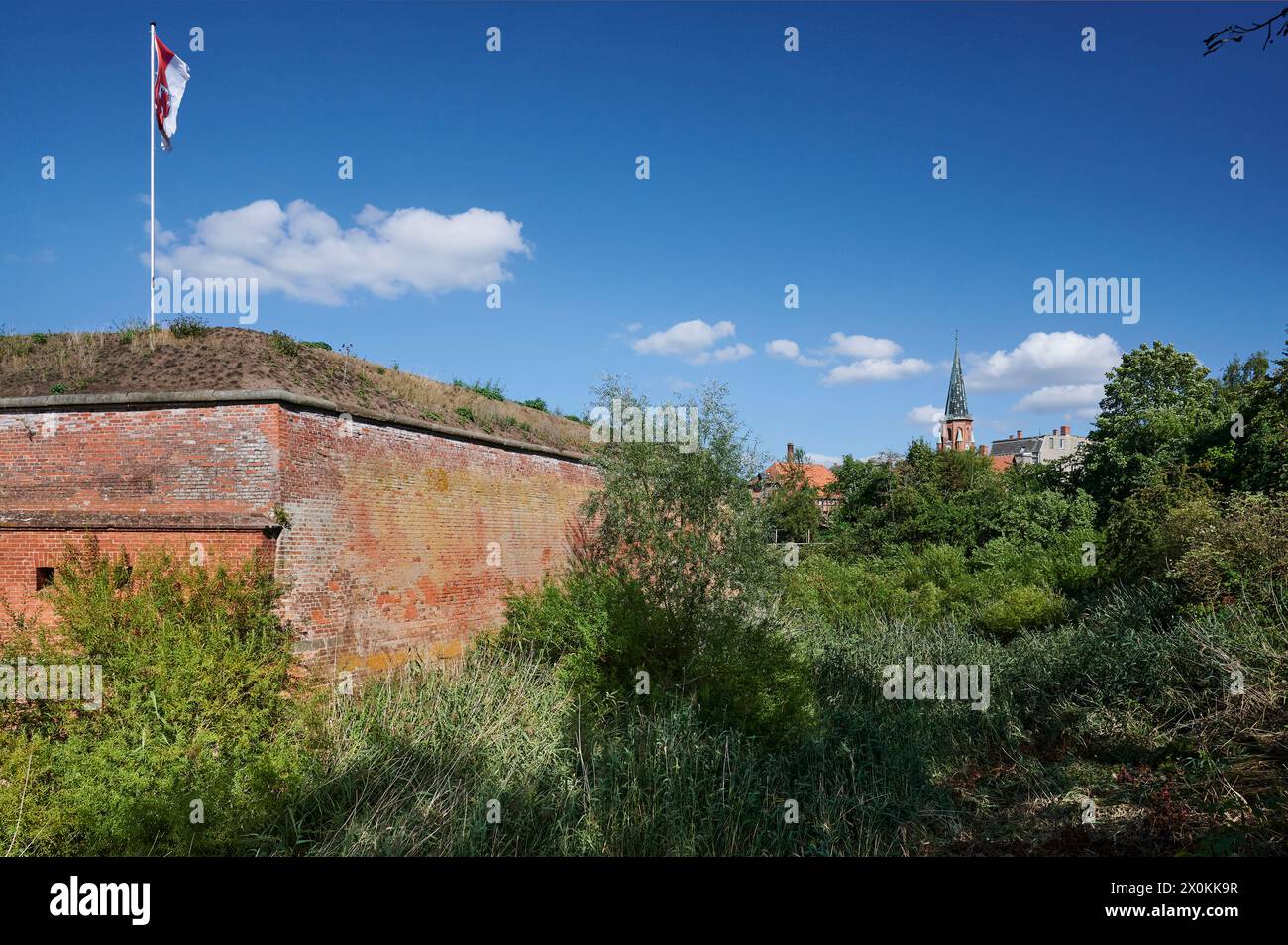 Castle wall of the Dömitz Citadel fortress, moat with bushes and church ...