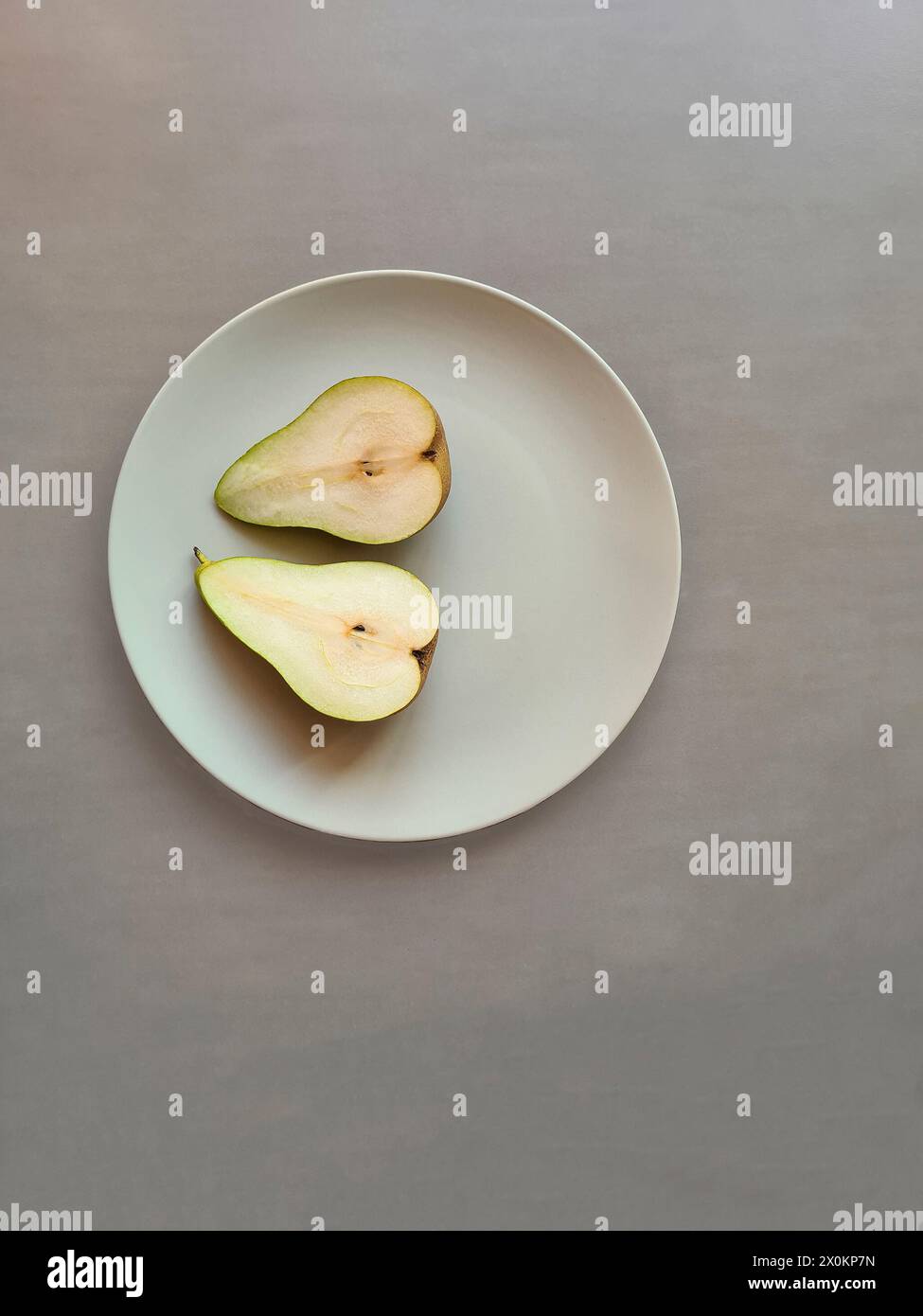 A halved pear with stem lies with both halves on a light gray plate ...