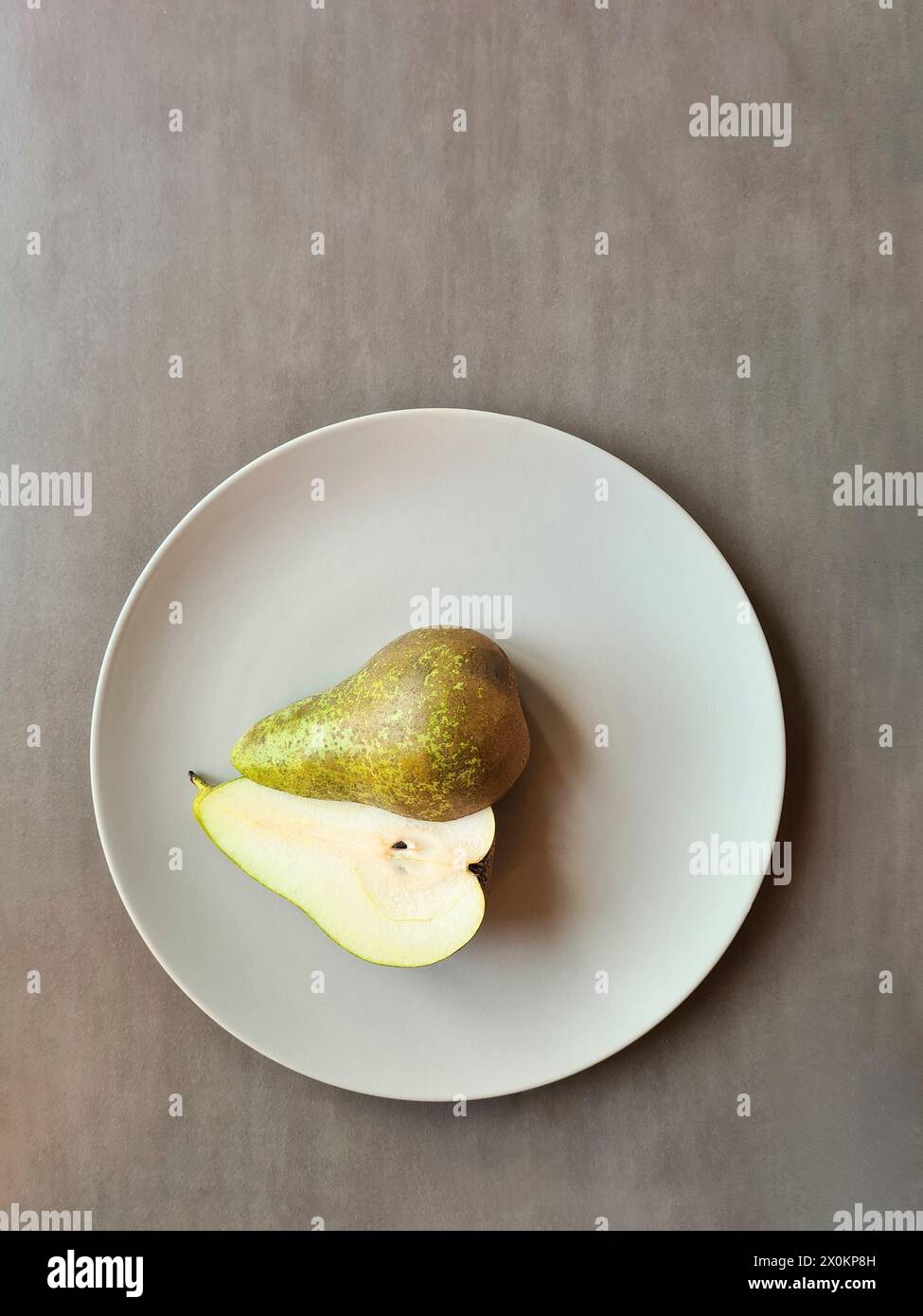 A halved pear with stem lies with both halves on a light gray plate ...