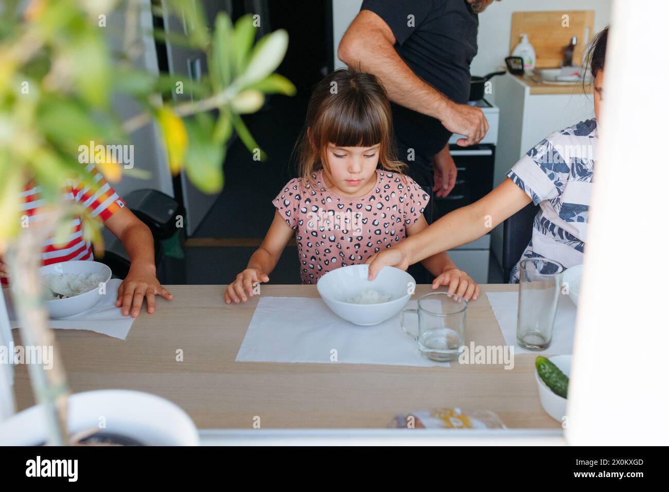 three children eating lunch at home at white table with father cooking ...