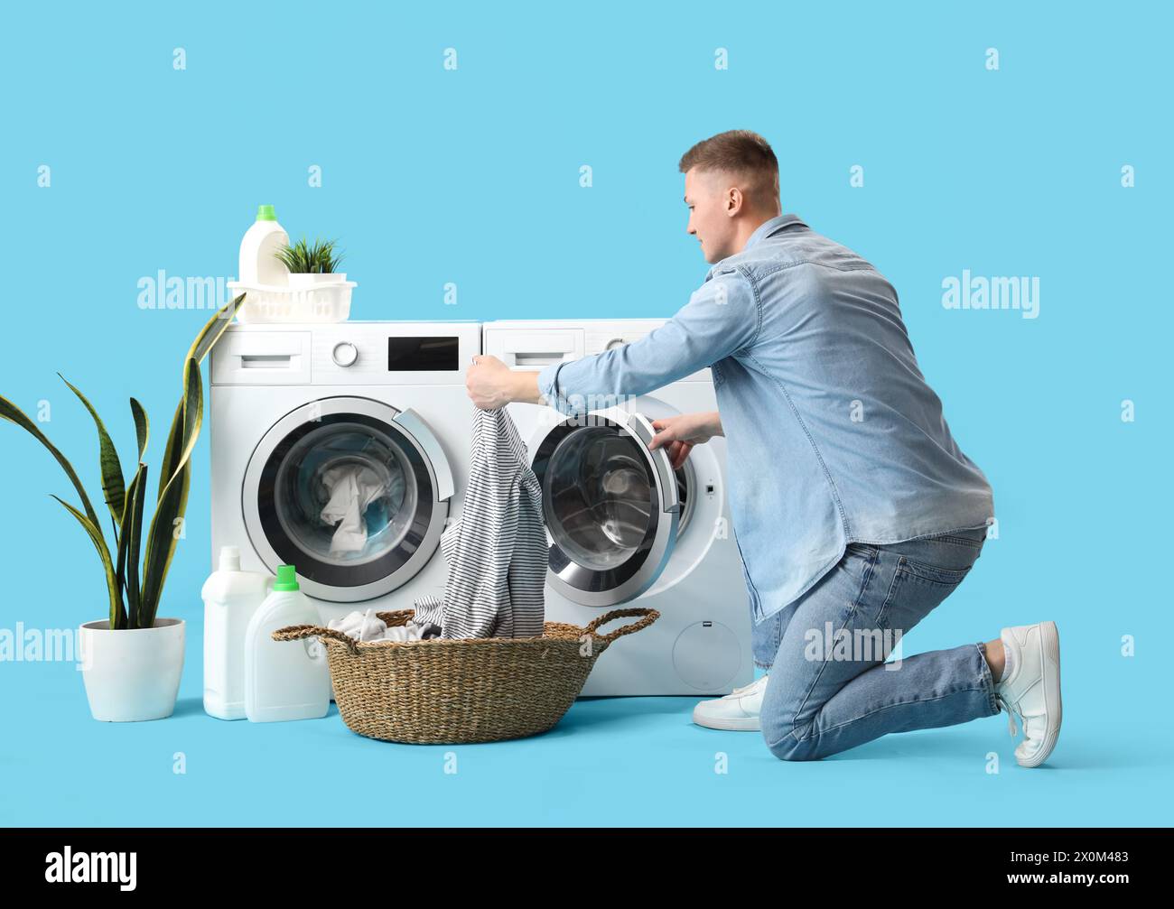 Handsome young man putting laundry into washing machine on blue ...
