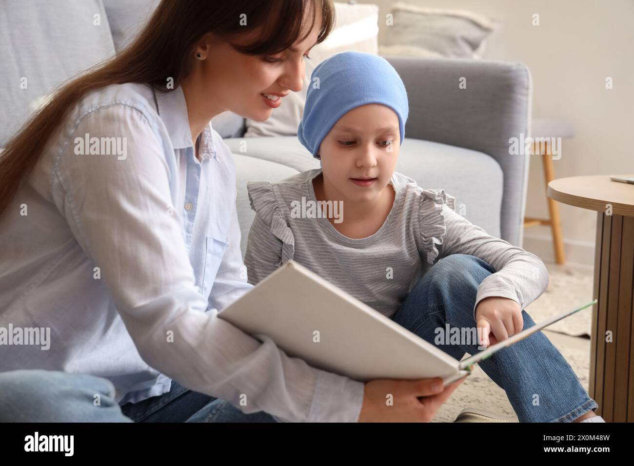 Little girl after chemotherapy with her mother reading story at home ...