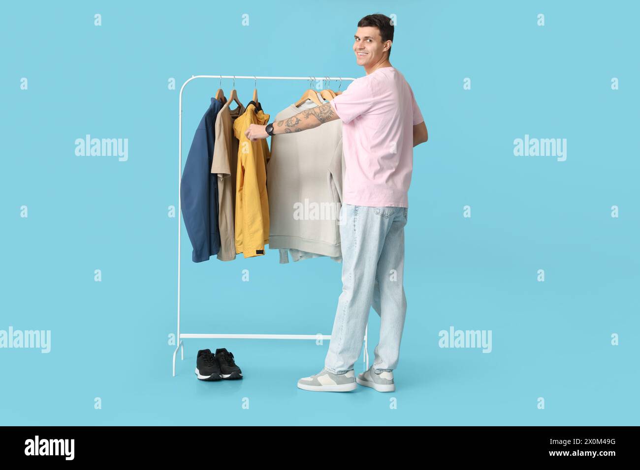 Handsome young man and rack with stylish clothes on blue background ...