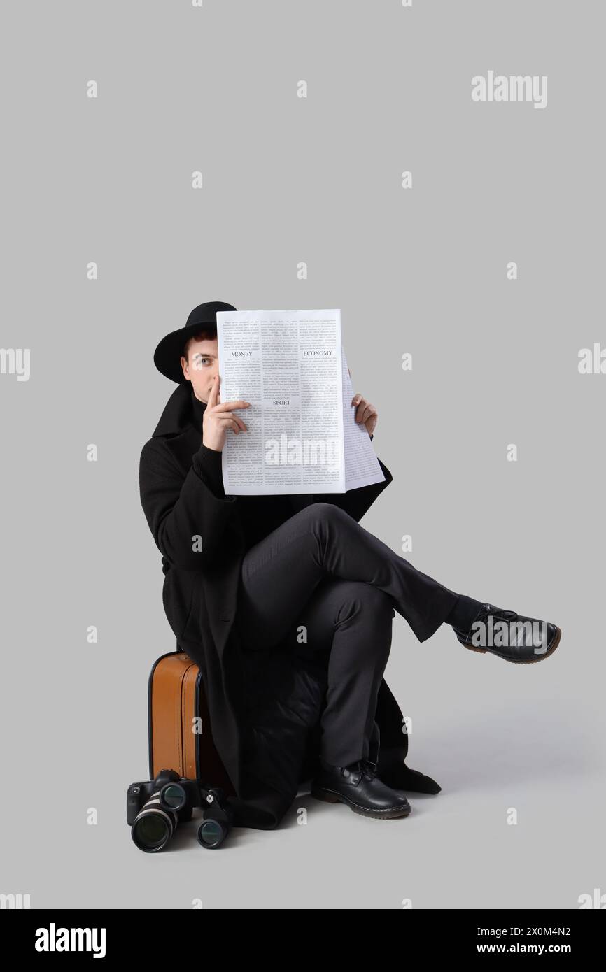 Male spy with newspaper sitting on bag against light background Stock ...