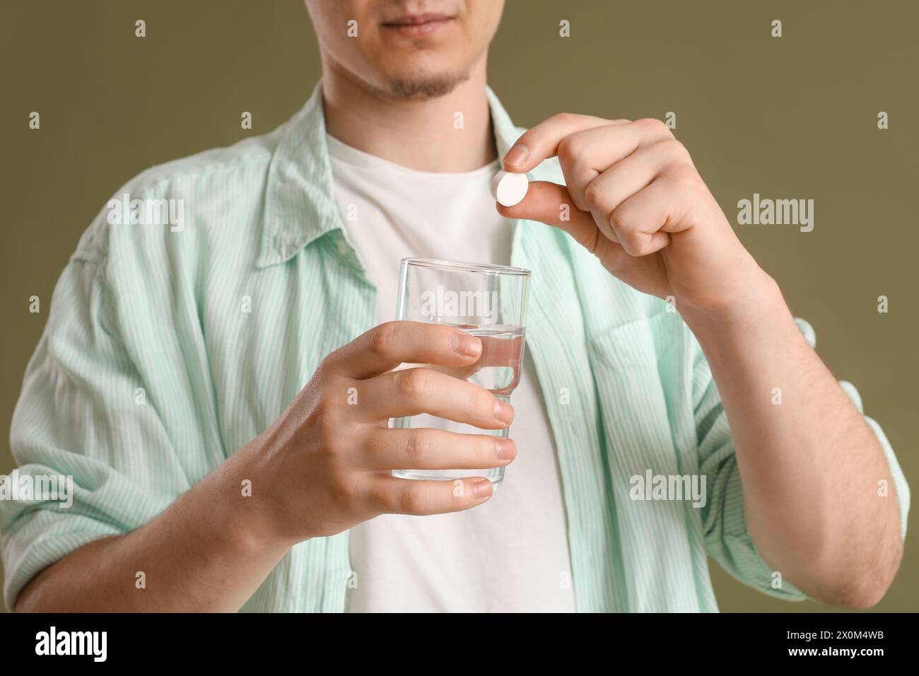 Man putting soluble tablet for headache into glass of water on green ...