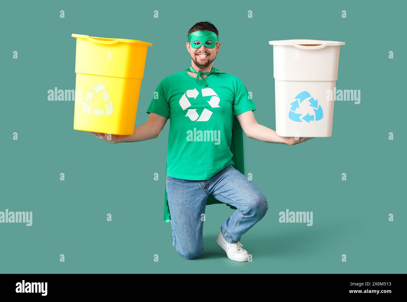 Young man dressed as eco superhero with garbage bins on green ...