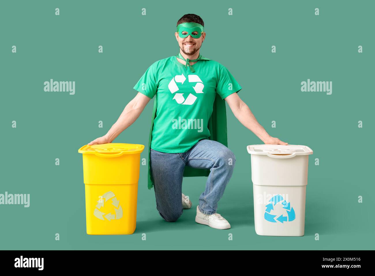 Young man dressed as eco superhero with garbage bins on green ...