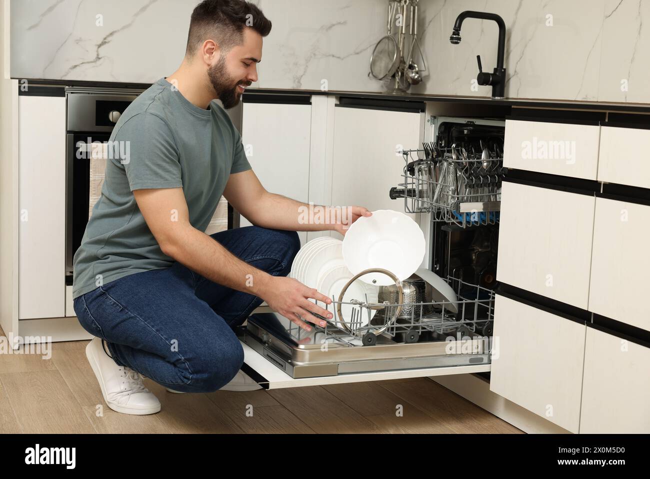 Smiling man loading dishwasher with plates in kitchen Stock Photo - Alamy