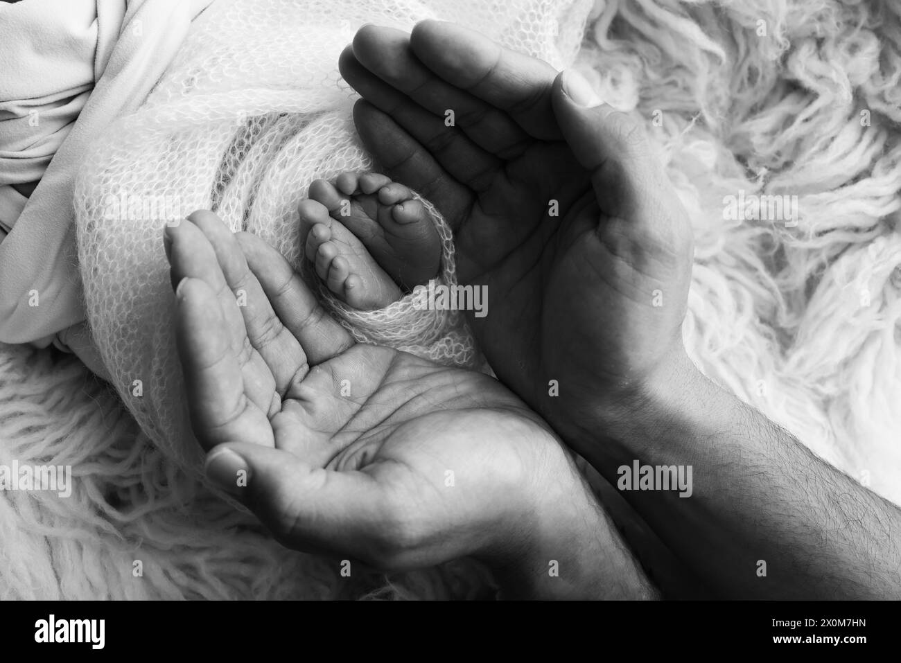 The palms of the father, the mother are holding the foot of the newborn ...