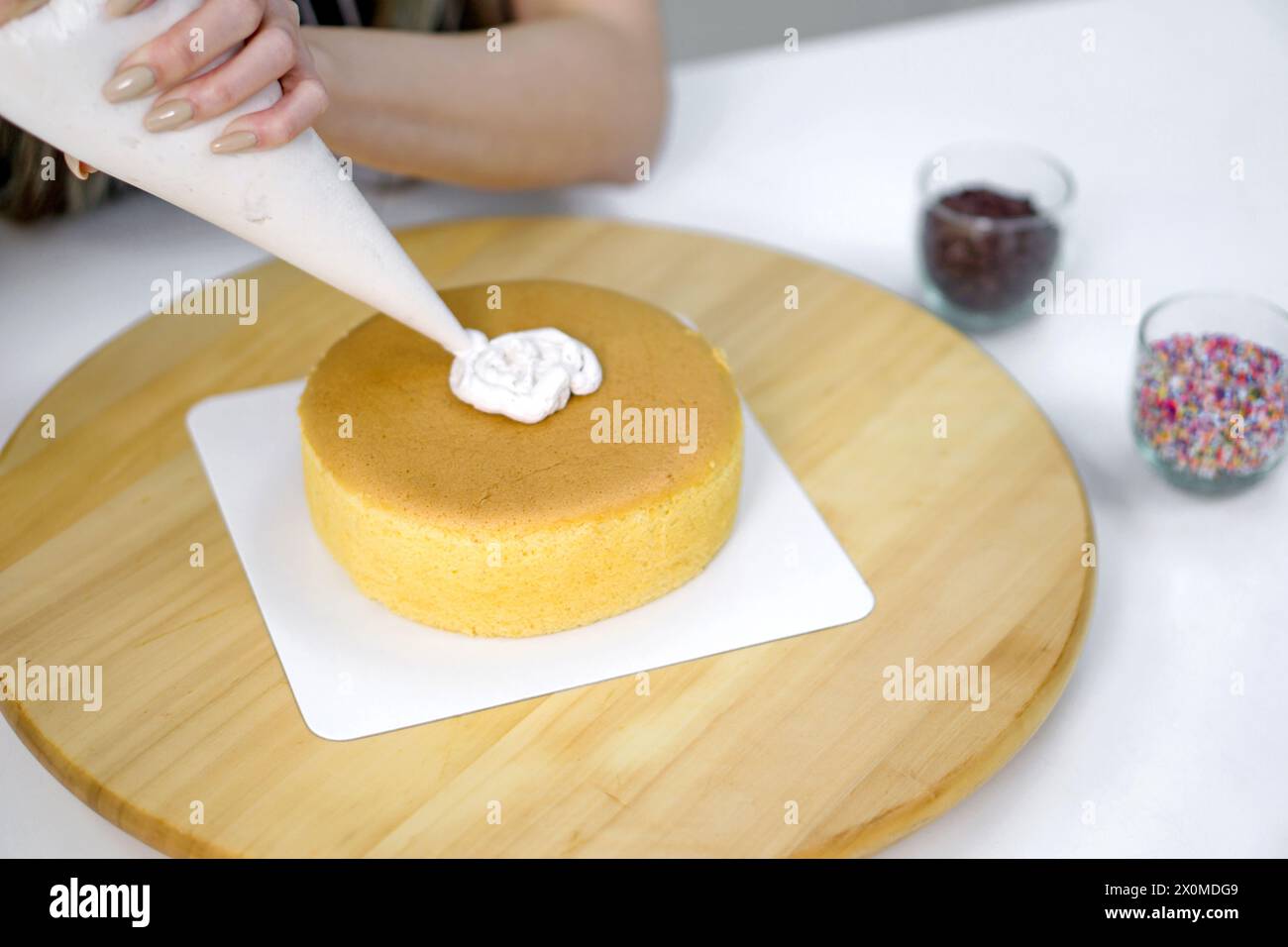 Closeup hand piping white cream on a sponge cake, creating a decorative ...