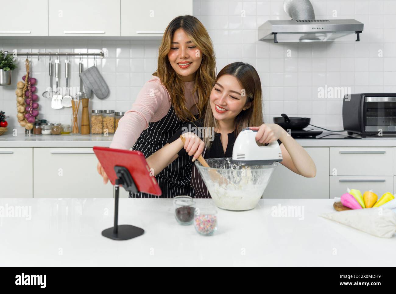 Two women in an apron, smiling and baking together in a kitchen with a ...