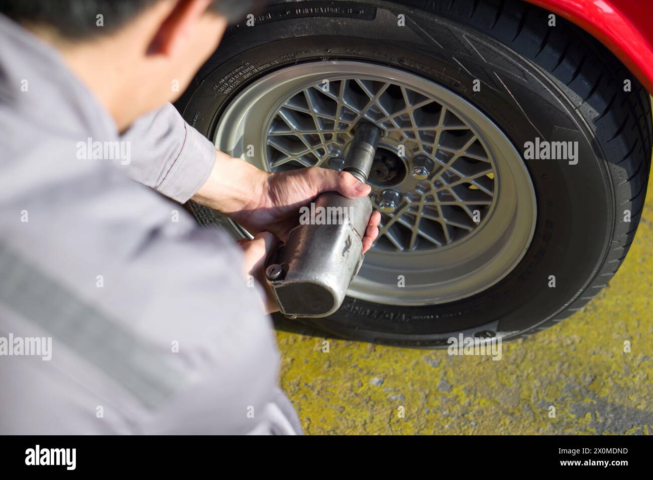 A mechanic in uniform using a pneumatic impact wrench to work on a car ...