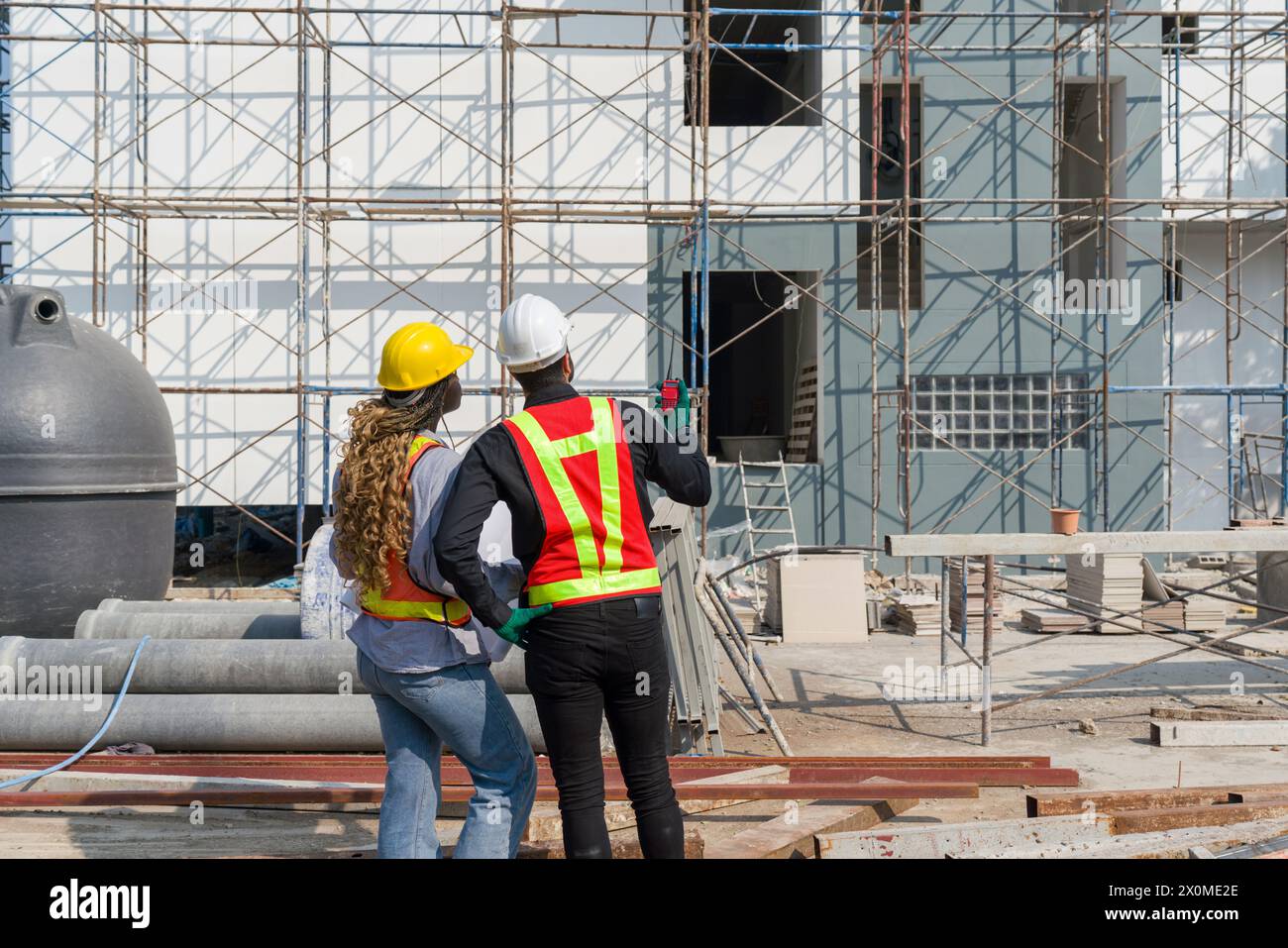 Two construction workers are standing together in front of a large ...