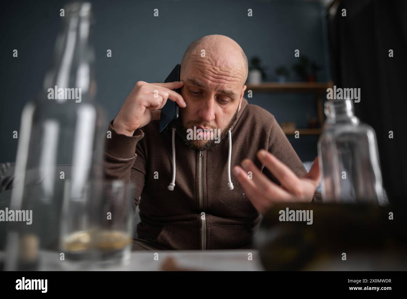 Boozy male alcoholic drinking whiskey and calling on smartphone at home ...