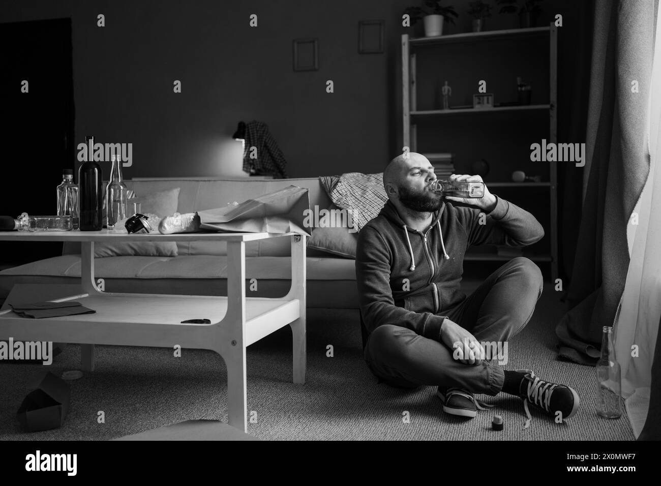 Male alcoholic with bottle of whiskey sitting on floor, black and white ...