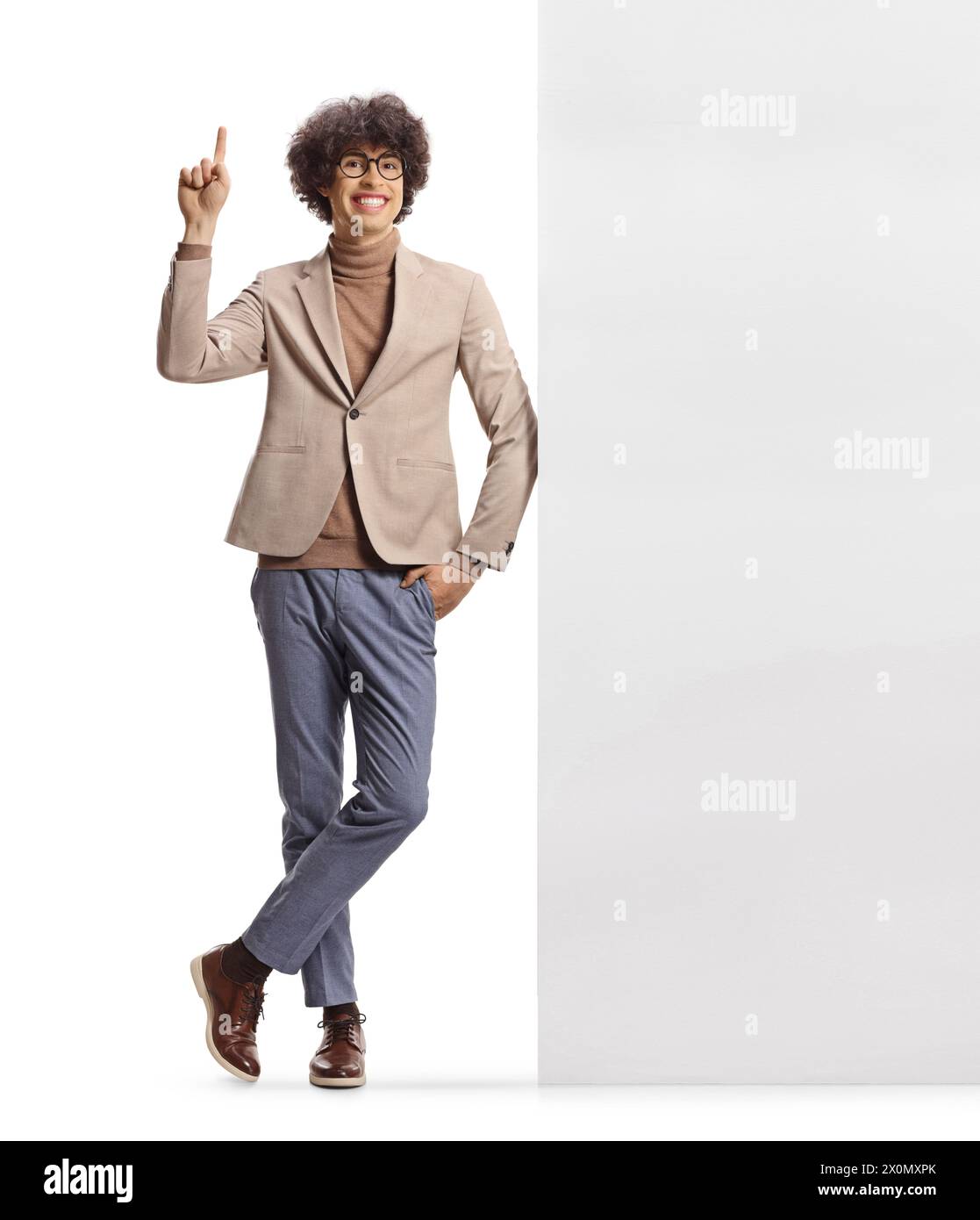Tall young man with curly hair leaning on a wall and pointing up ...