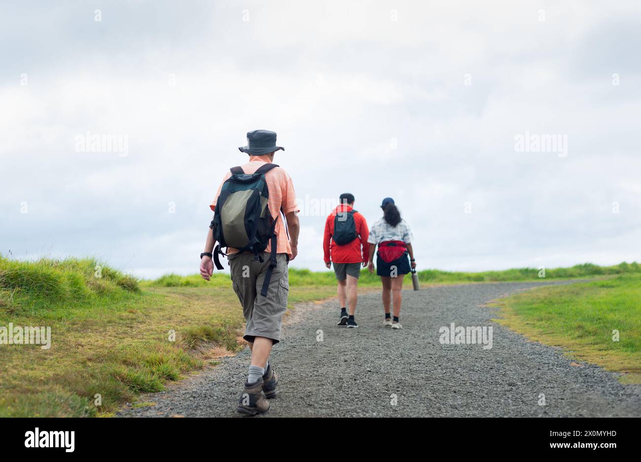 Three people walking uphill under a cloudy sky. Long Bay Coastal Okura ...