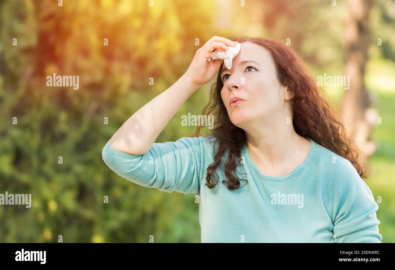 Stressed woman drying sweat using a wipe in a warm summer day in a park ...