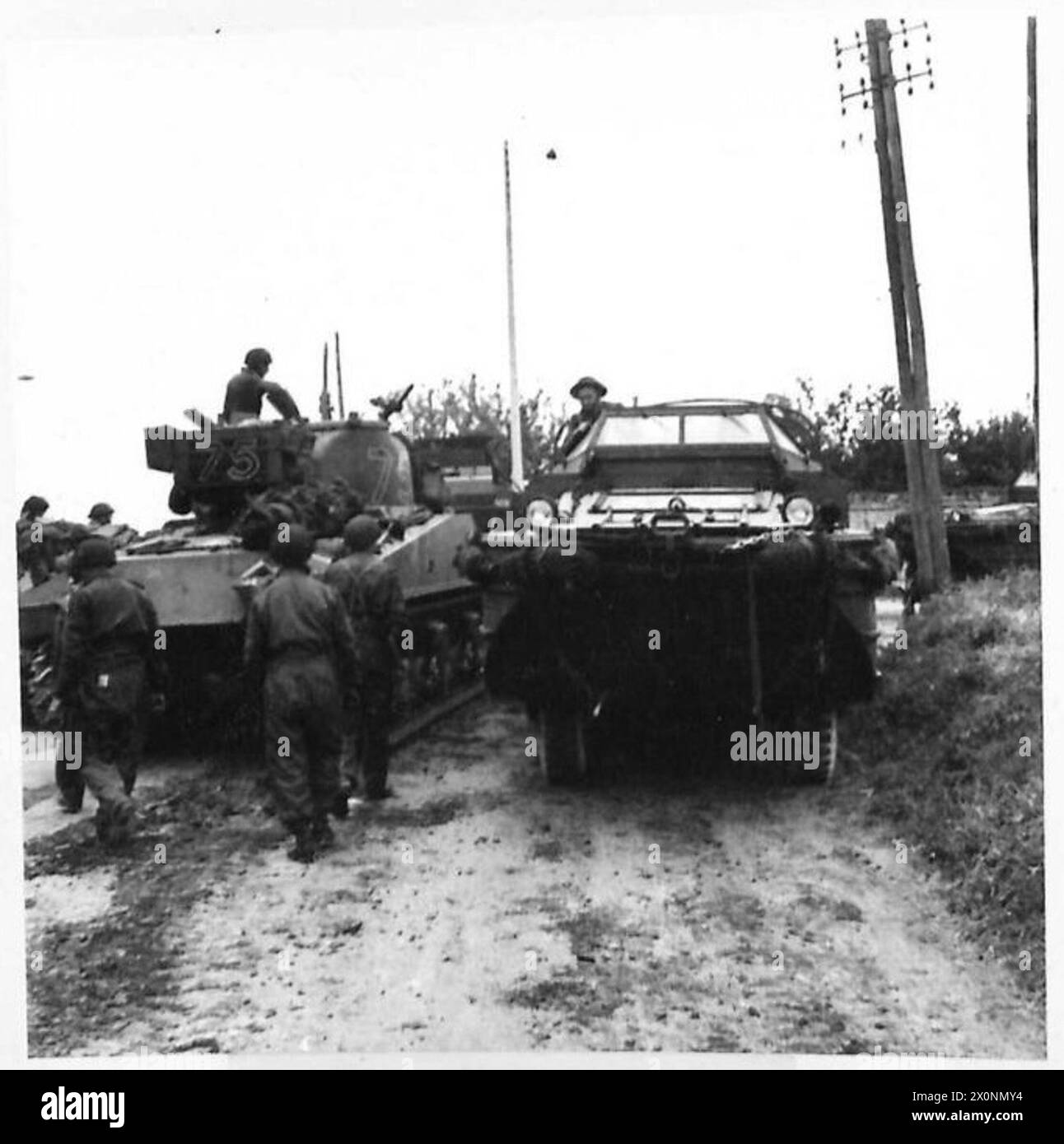 A Sherman tank of the 13th/18th Royal Hussars is shown passing DUKWs ...