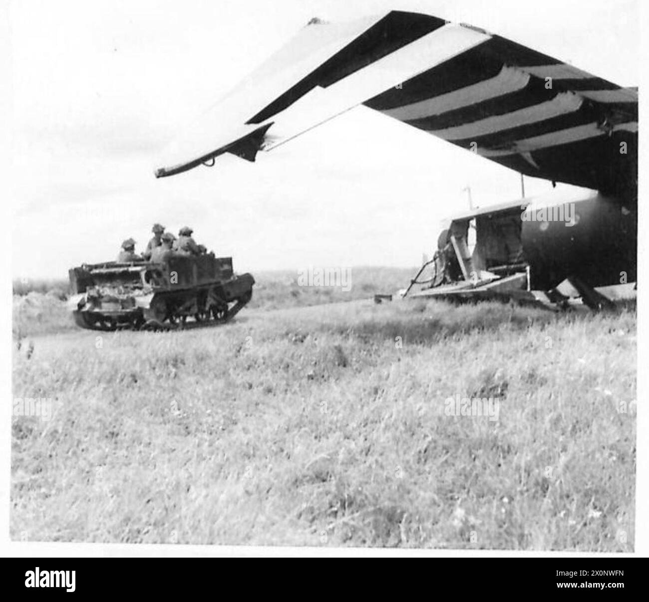 Photograph shows British troops in a Universal Carrier passing a Horsa ...