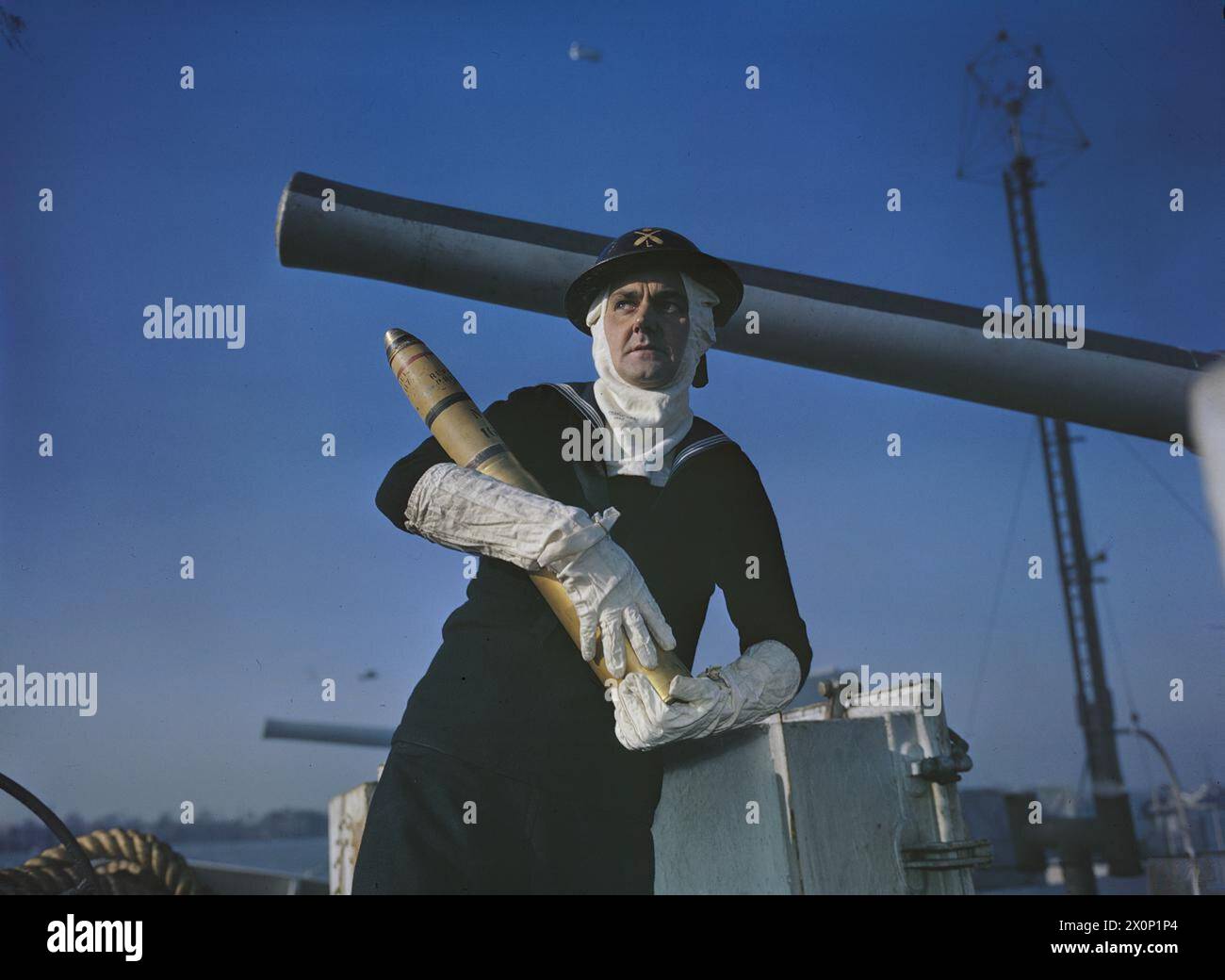 A naval gunner wearing anti-flash gear holds a shell aboard a Royal ...