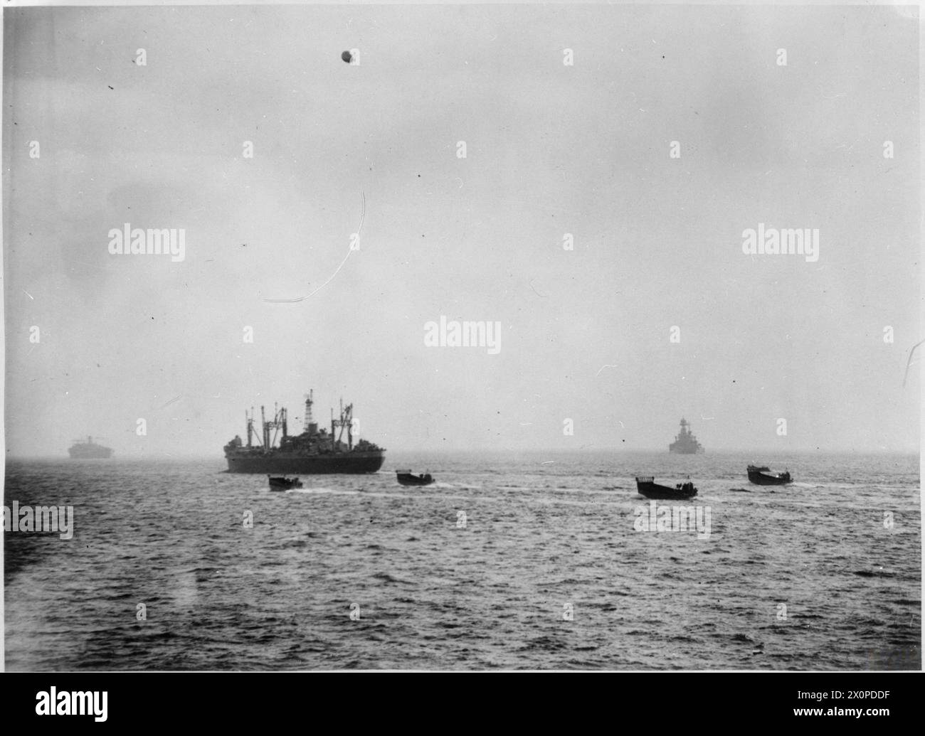 An assault ship with assault craft advances toward beaches, passing the ...