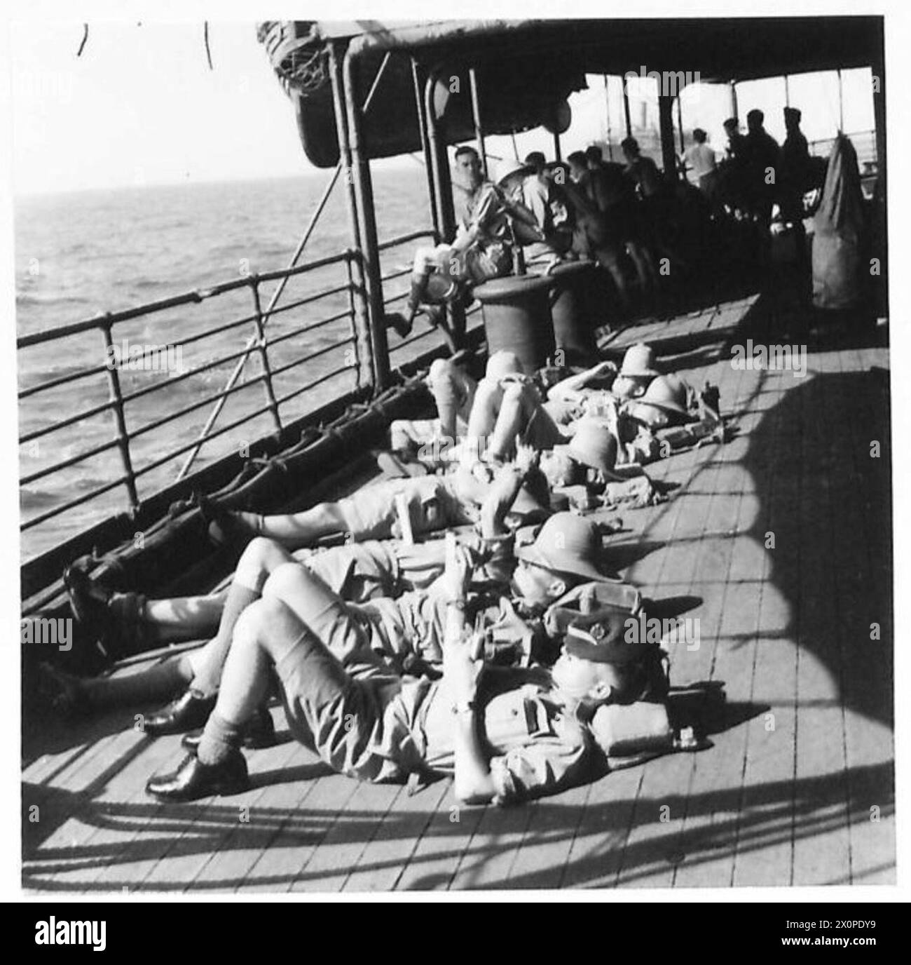 Photograph shows troops relaxing on a deck of a troop ship in a convoy ...