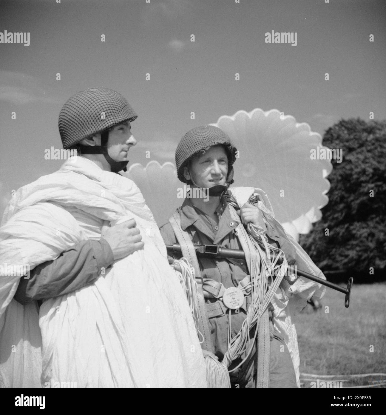 Two paratroopers carry their parachutes after a drop during training ...