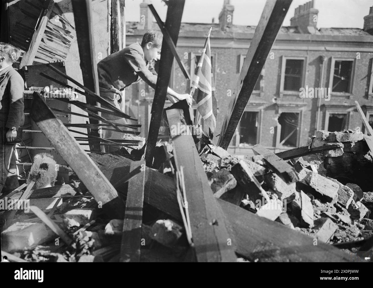 A young boy plants a Union Flag in the rubble of his destroyed home ...
