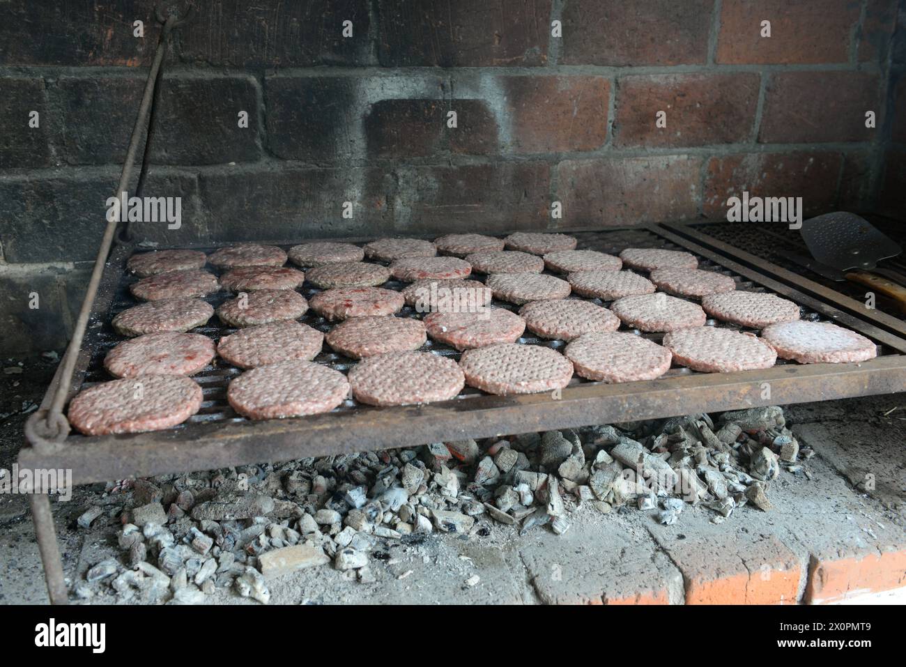 A grill full of hamburgers is cooking on a brick oven. The burgers are ...