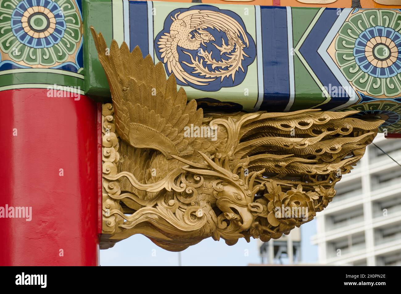 A gold and red bird is carved into a red and blue wooden structure. The ...